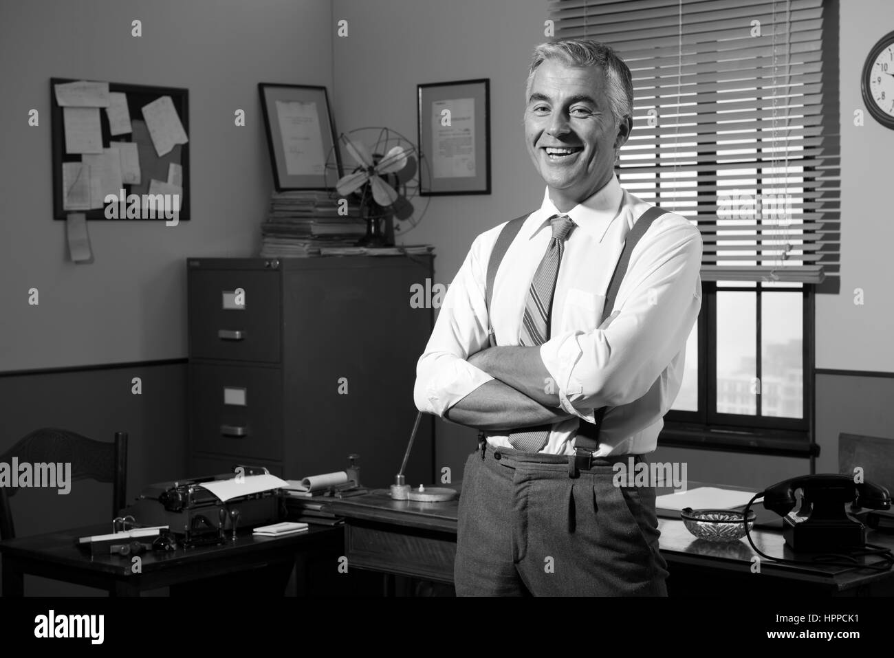 Confident smiling businessman with arms crossed, 1950s style office ...