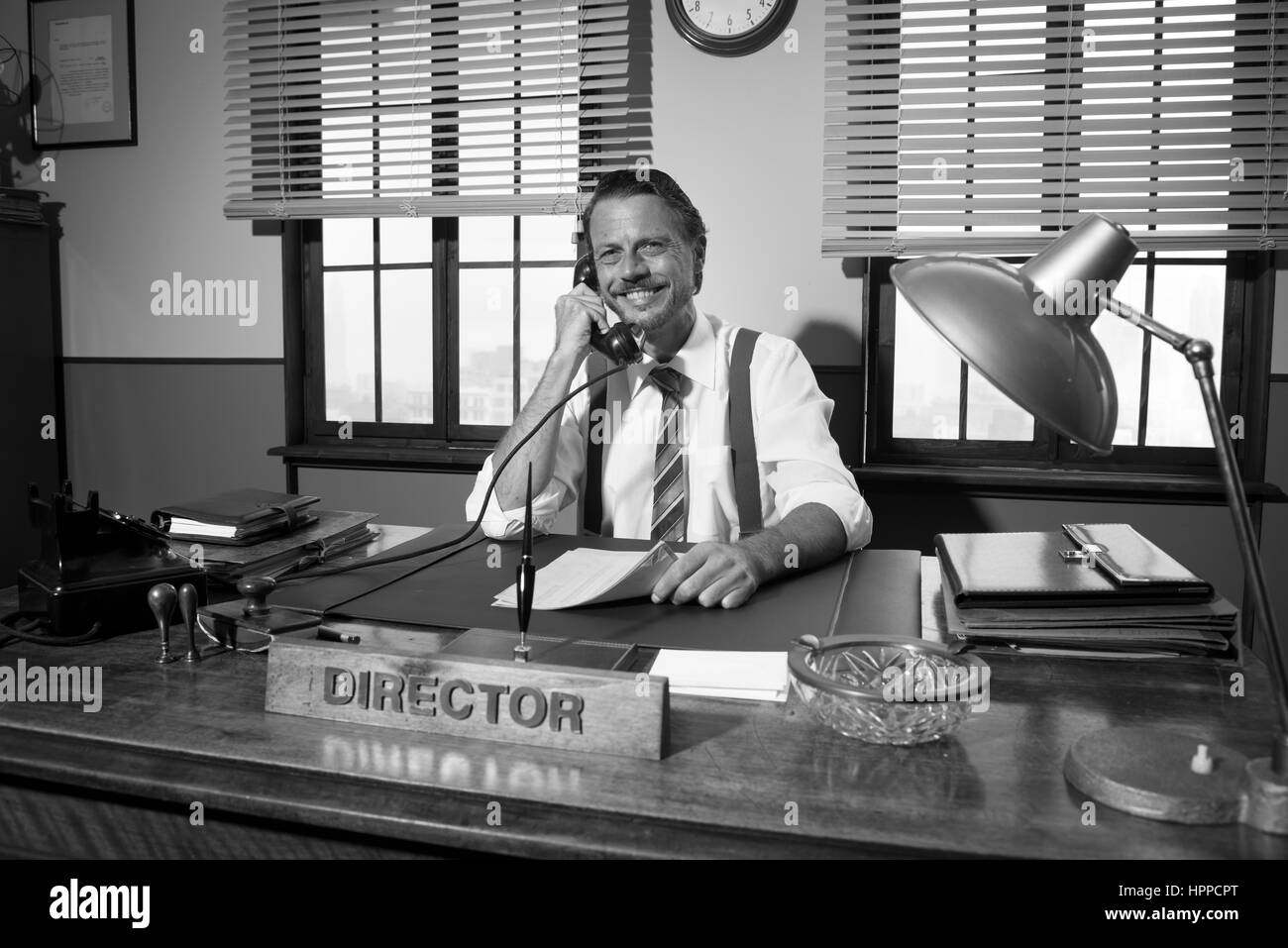 Smiling director working at desk having a phone call, 1950s style ...