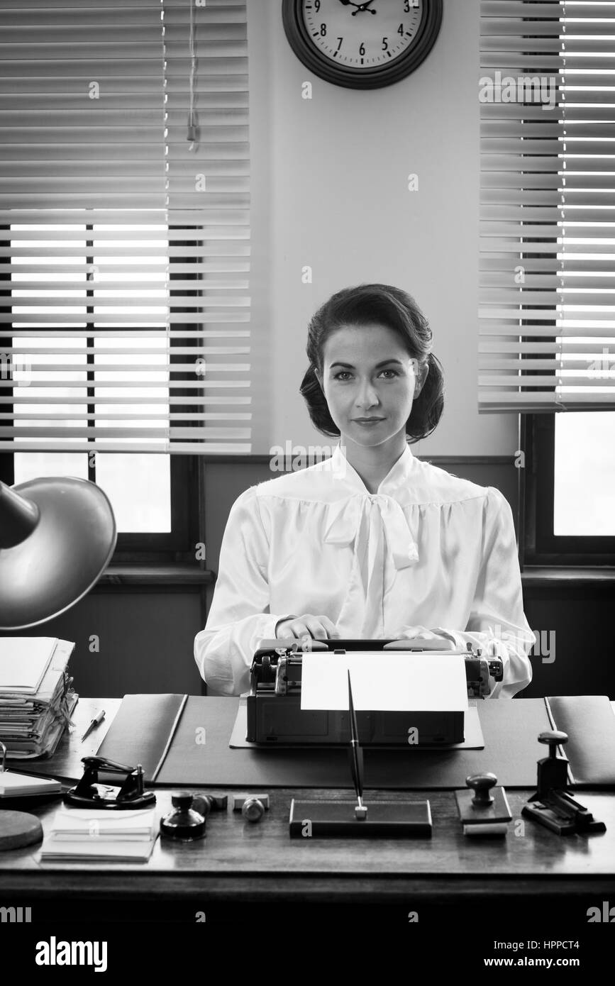 Smiling attractive secretary working at office typing on a typewriter ...