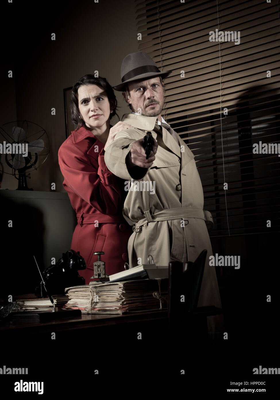 Brave detective pointing a gun and young scared woman hiding behind him ...