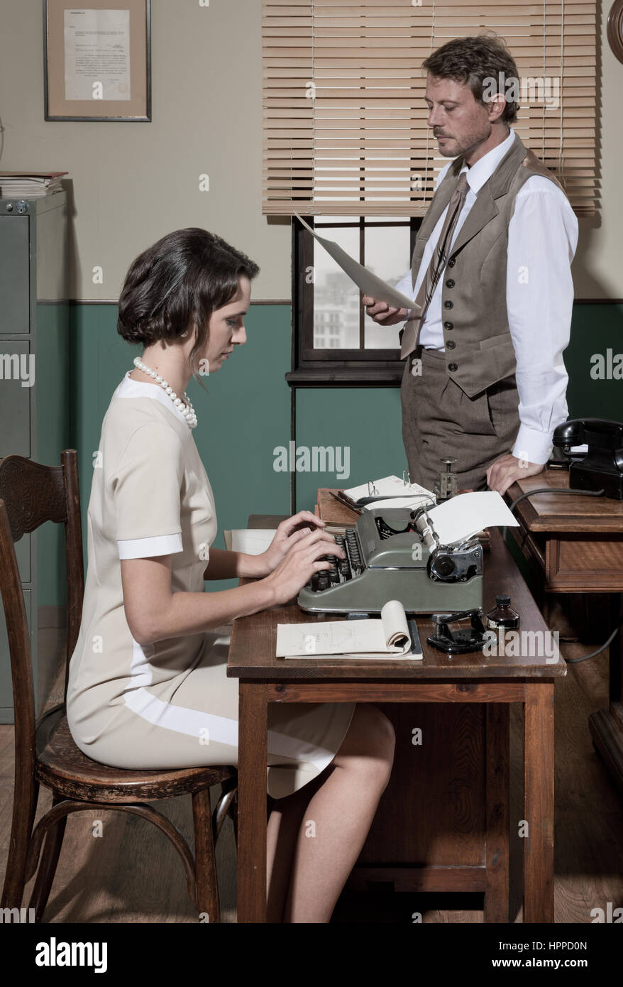 Director with paperwork and young secretary typing on typewriter in an ...