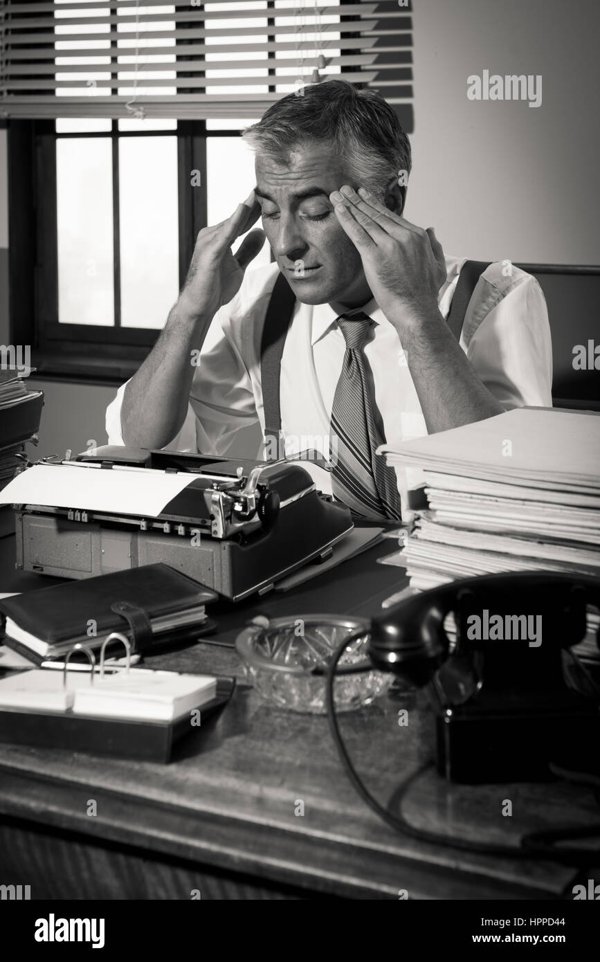 Exhausted reporter with headache working at office desk and touching ...