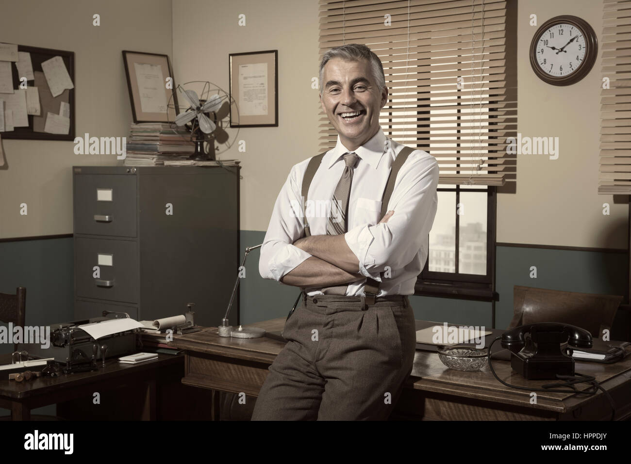 Confident smiling businessman with arms crossed, 1950s style office ...