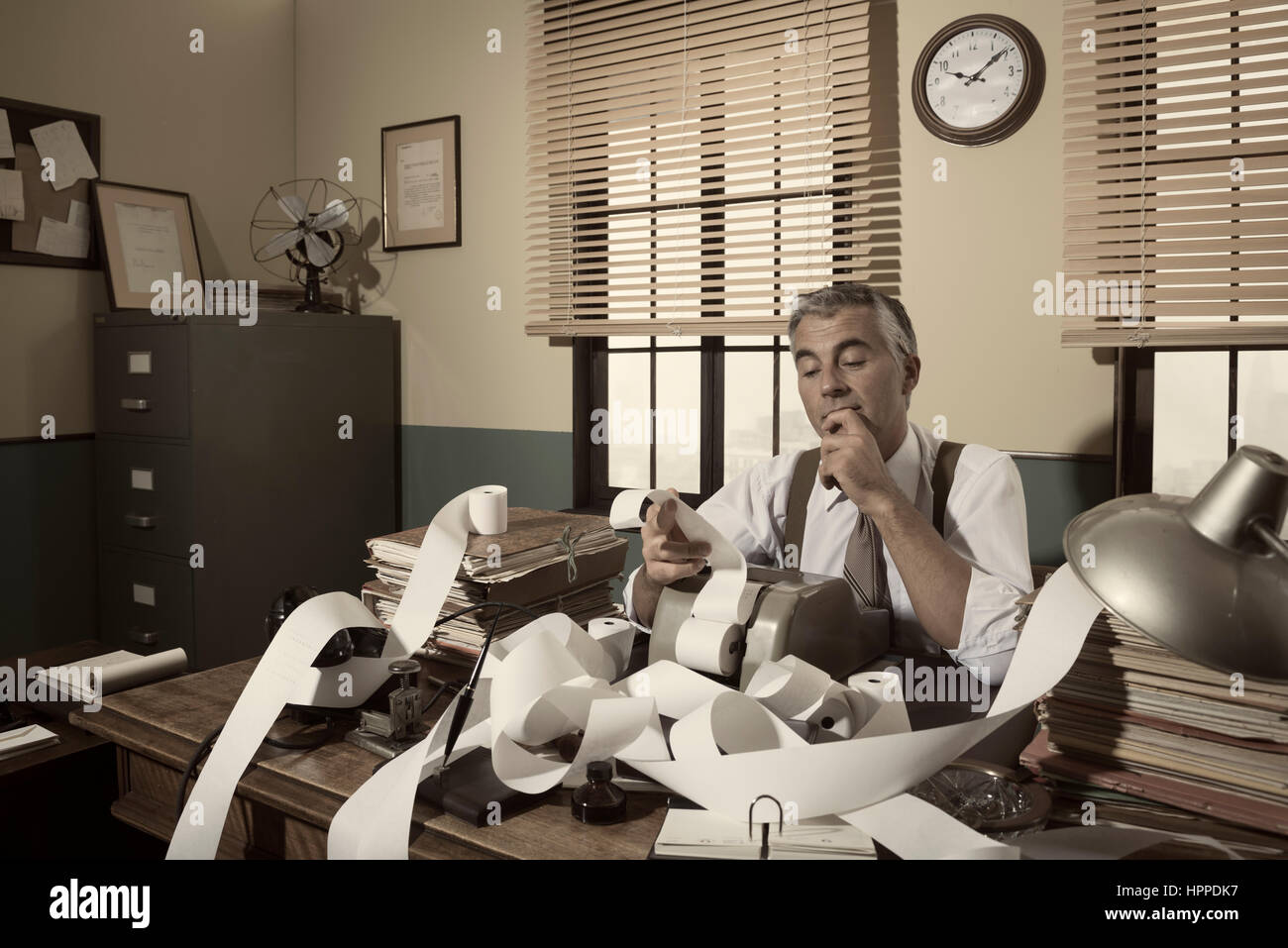 1950s accountant checking calculations in his office with hand on chin ...
