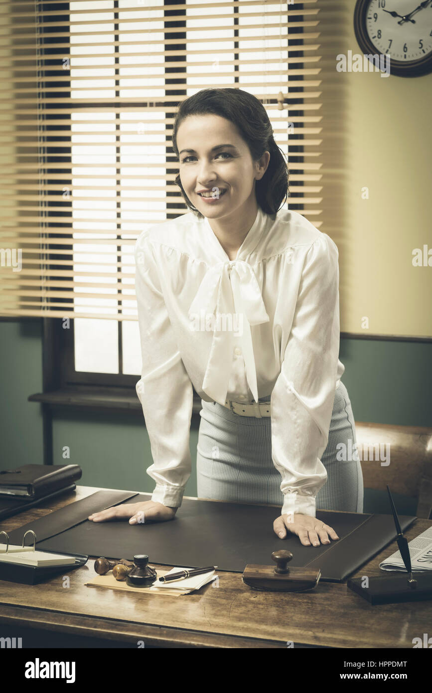 1950s smiling business woman leaning on office desk Stock Photo - Alamy