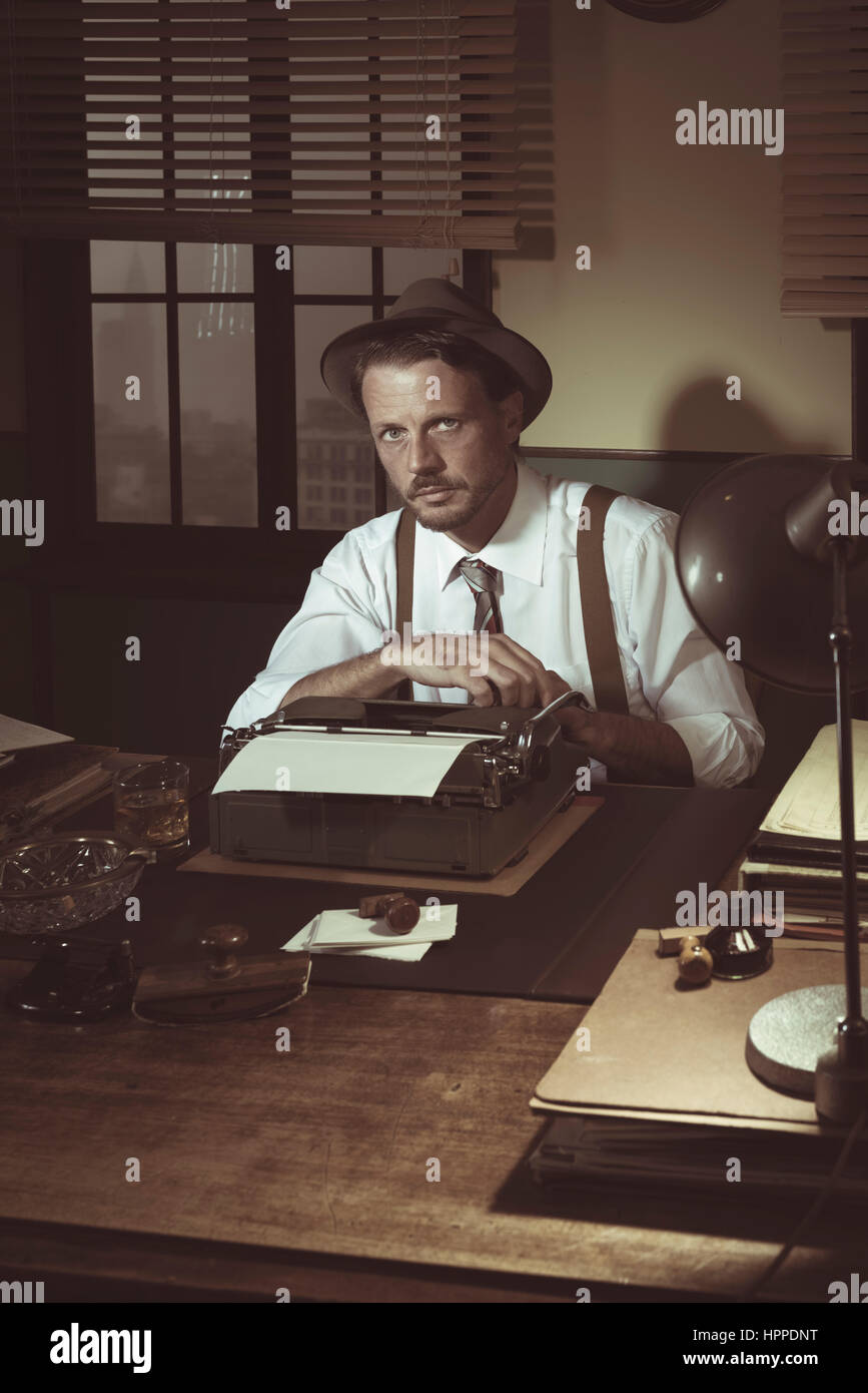 Retro reporter sitting at desk with typewriter posing and looking at ...