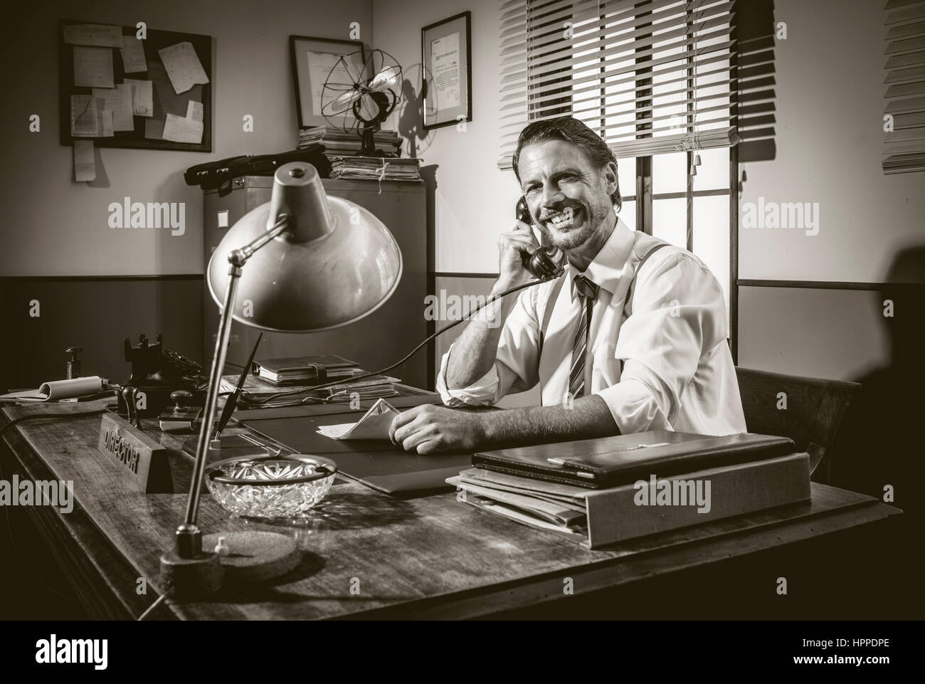 Smiling director working at desk having a phone call, 1950s style ...