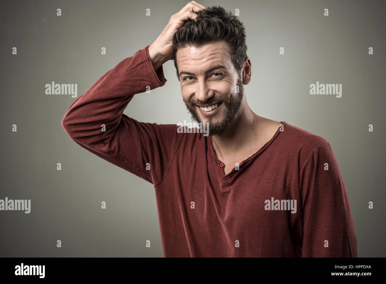 Doubtful smiling young man touching his head and thinking Stock Photo ...