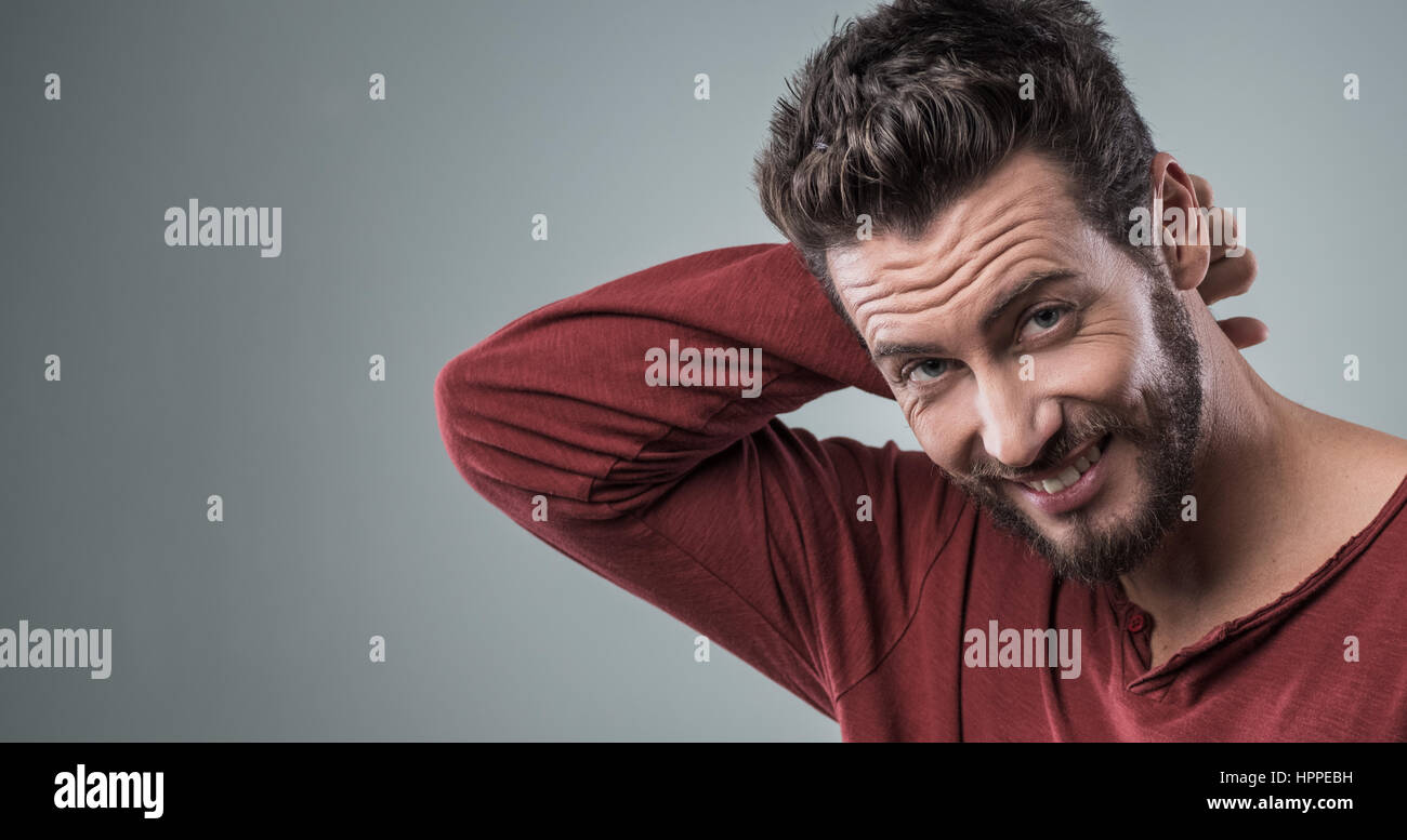 Shy attractive guy smiling at camera with hand behind head Stock Photo ...
