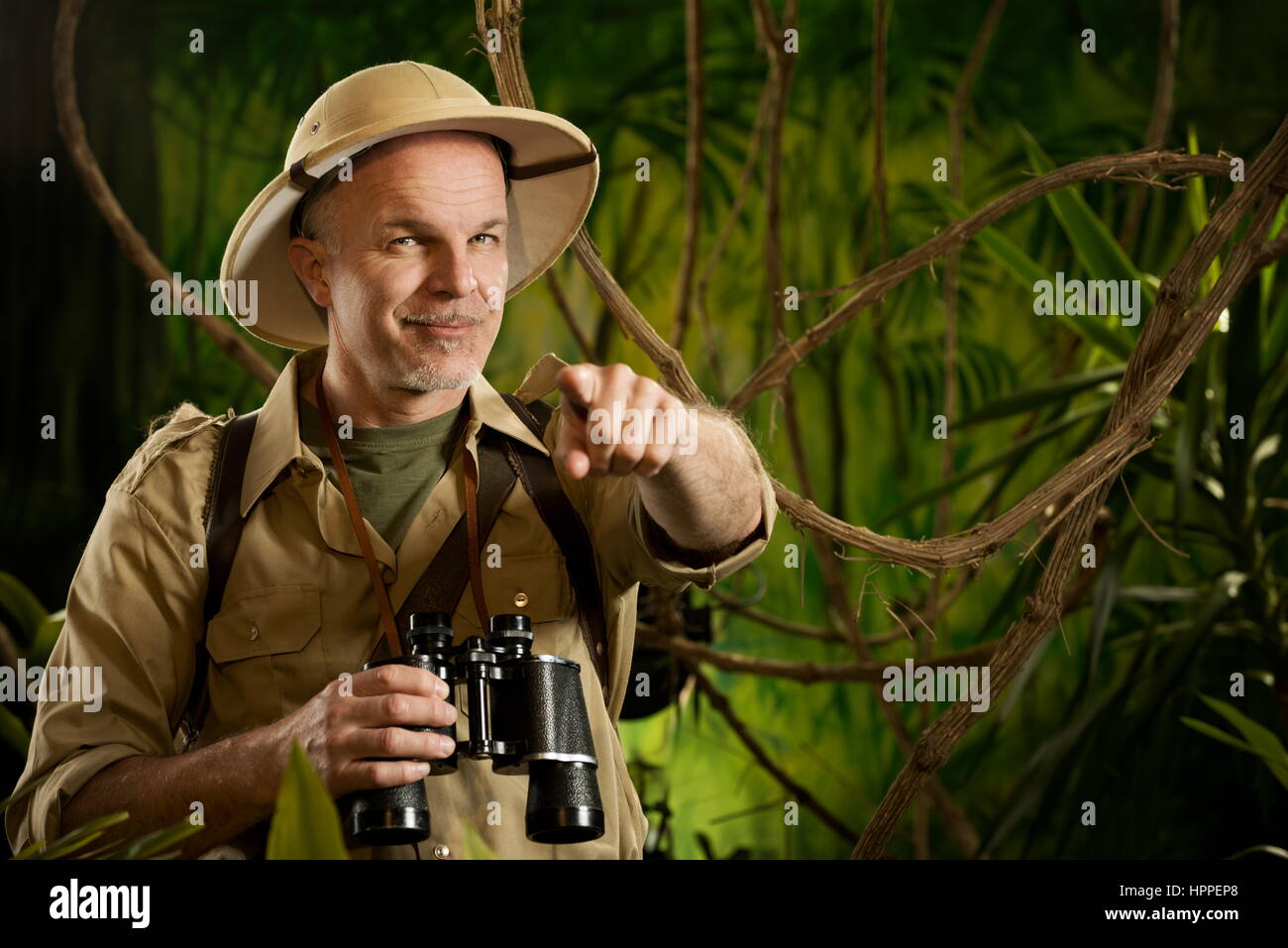 Smiling explorer in the jungle with binoculars pointing at camera Stock ...