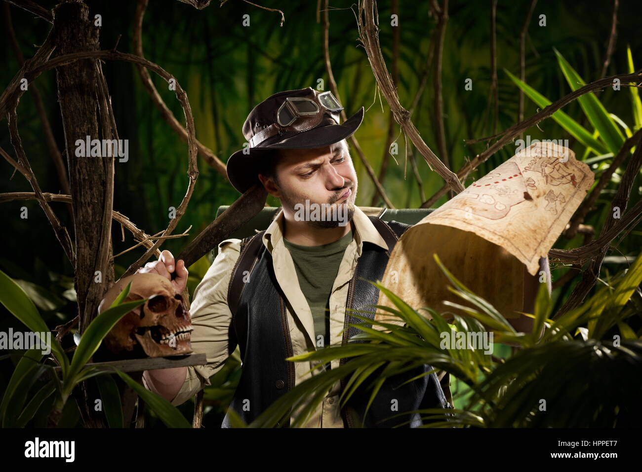 Lost explorer in the jungle holding an old map with skull on foreground ...