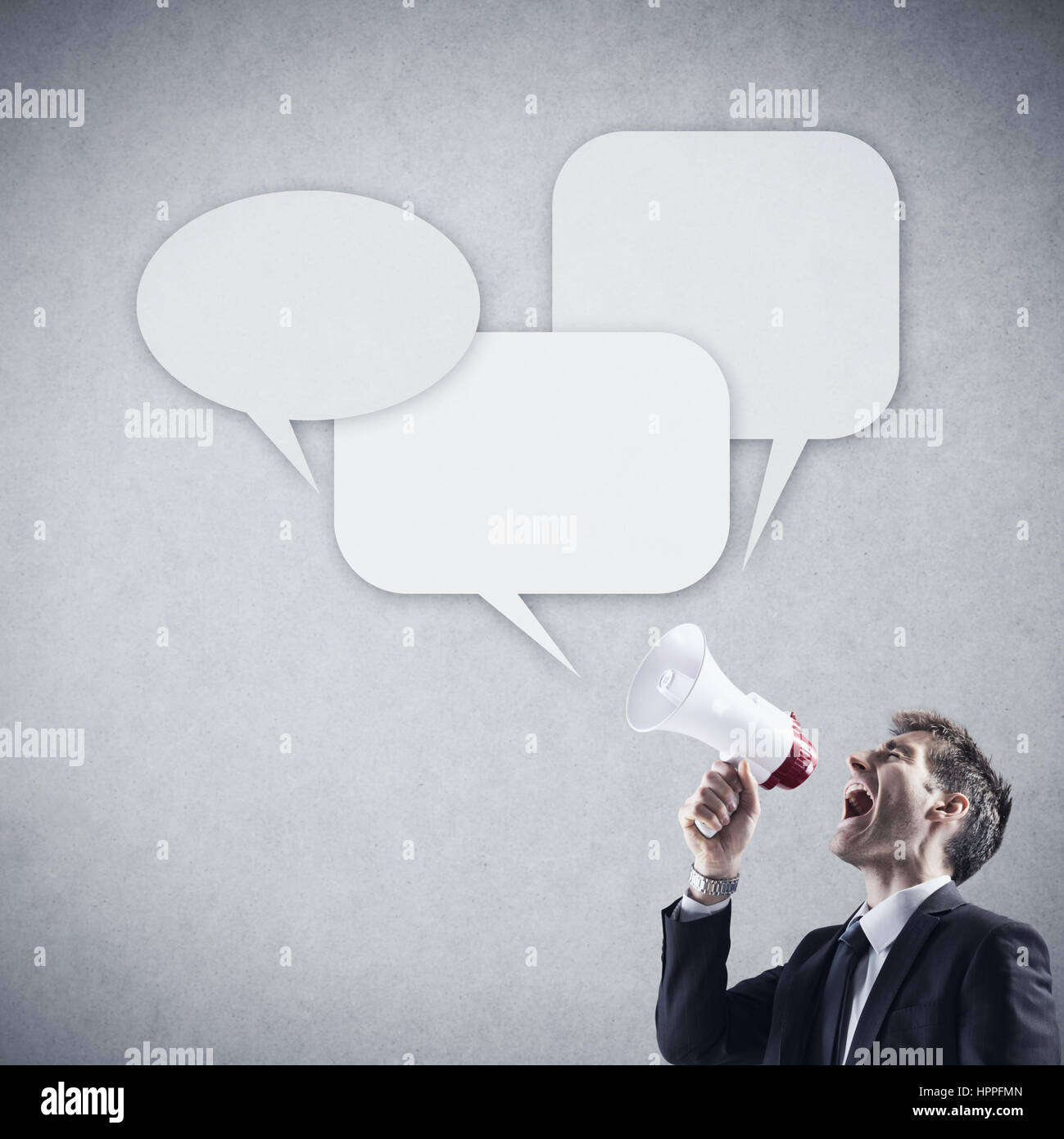 Angry young businessman shouting into megaphone against grey background ...