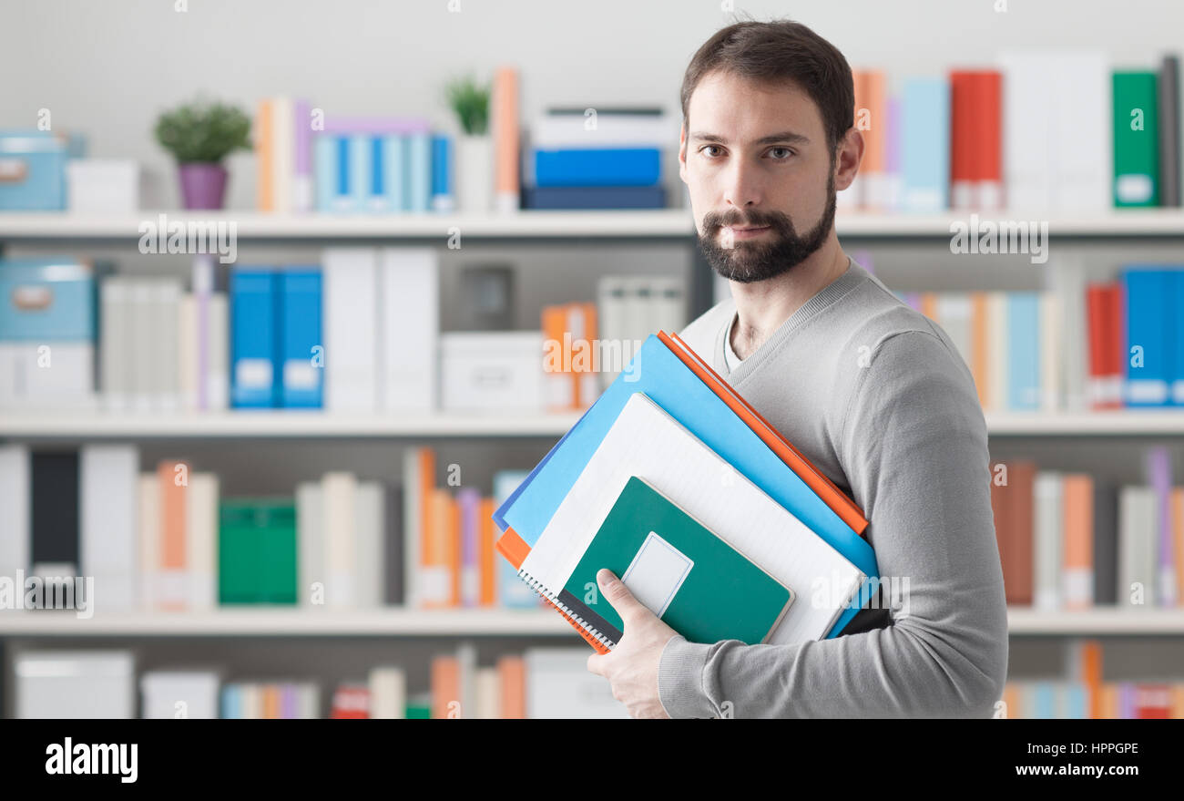 Man holding files and folders and smiling at camera, office shelves ...