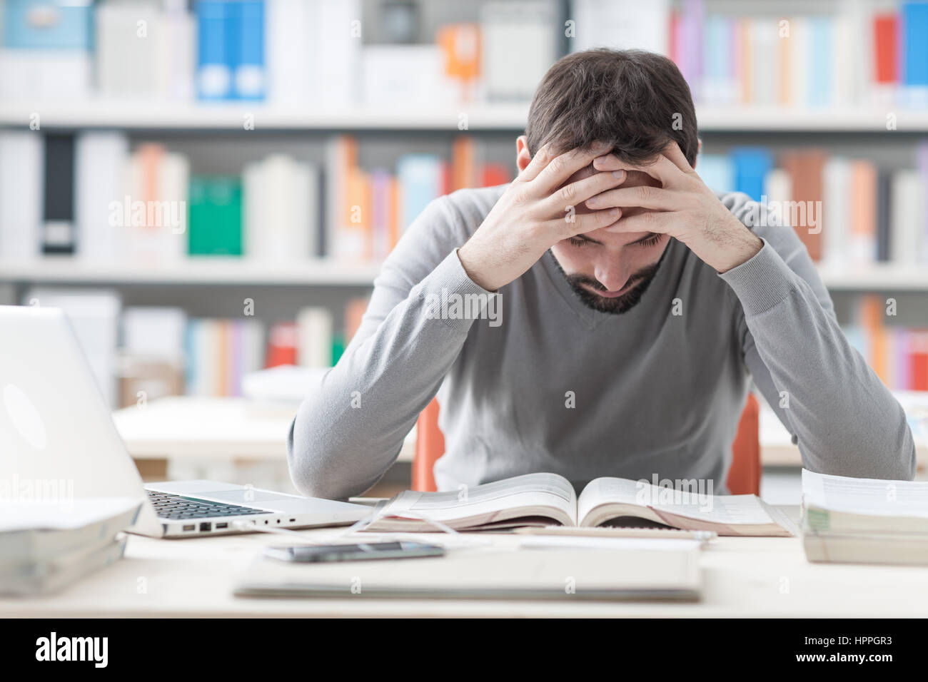 Exhausted young man working at office desk and touching his head, he is ...