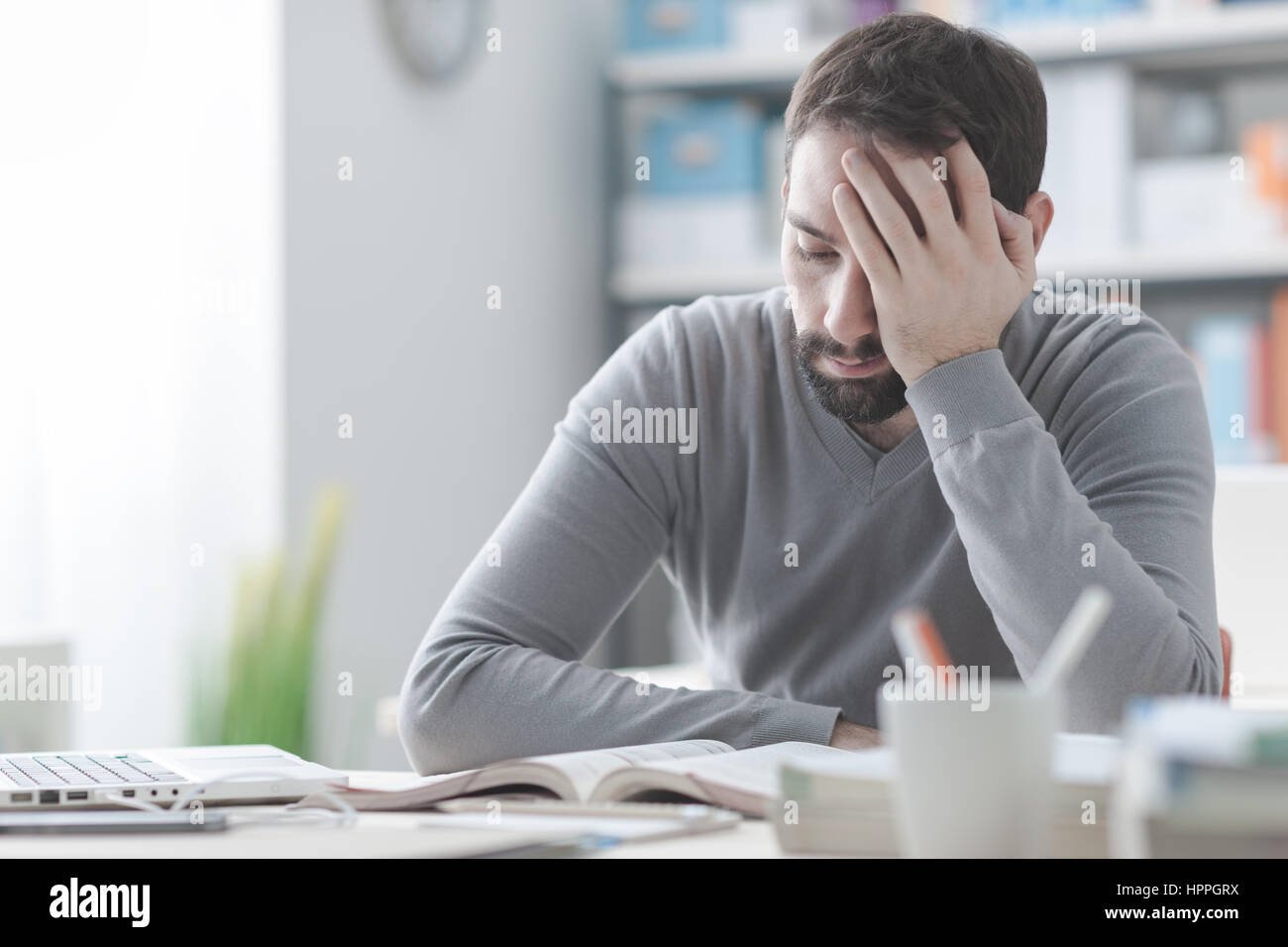 Exhausted young man working at office desk and touching his head, he is ...