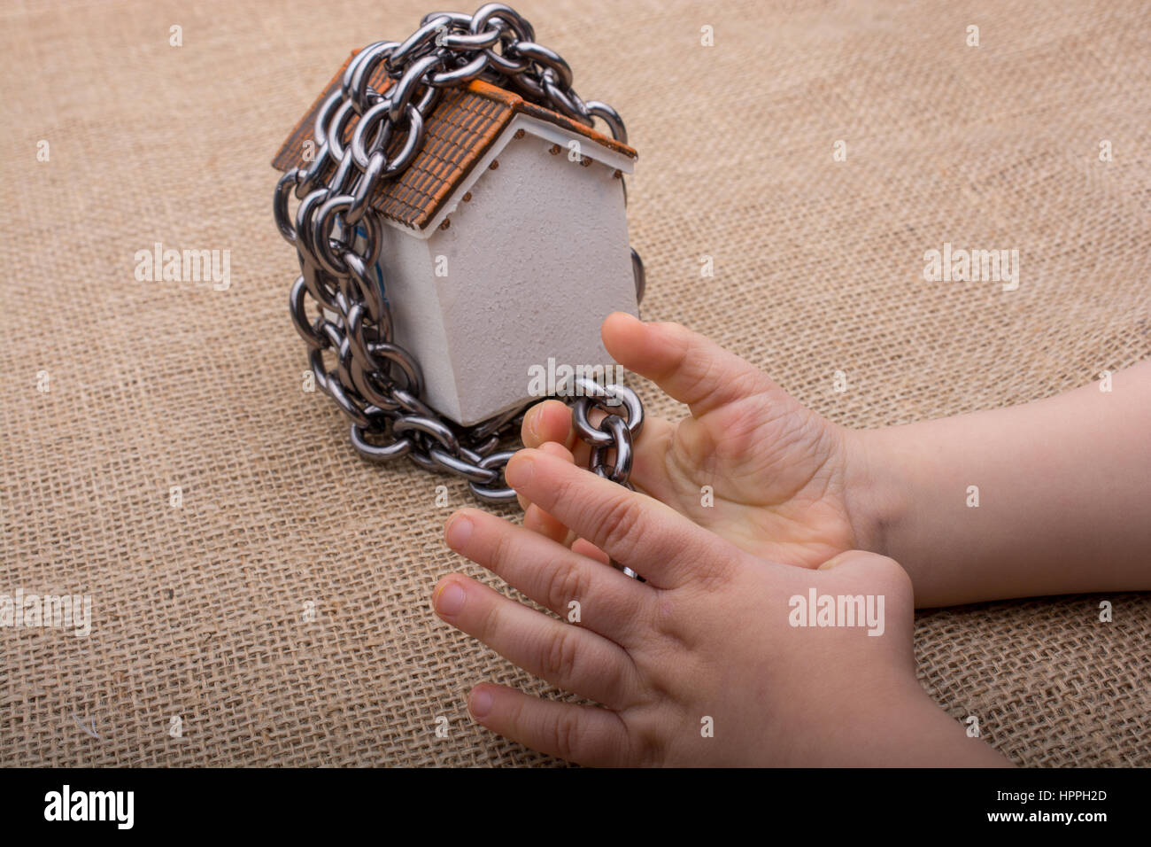 Little hand holding a chain around a model house on a brown background ...