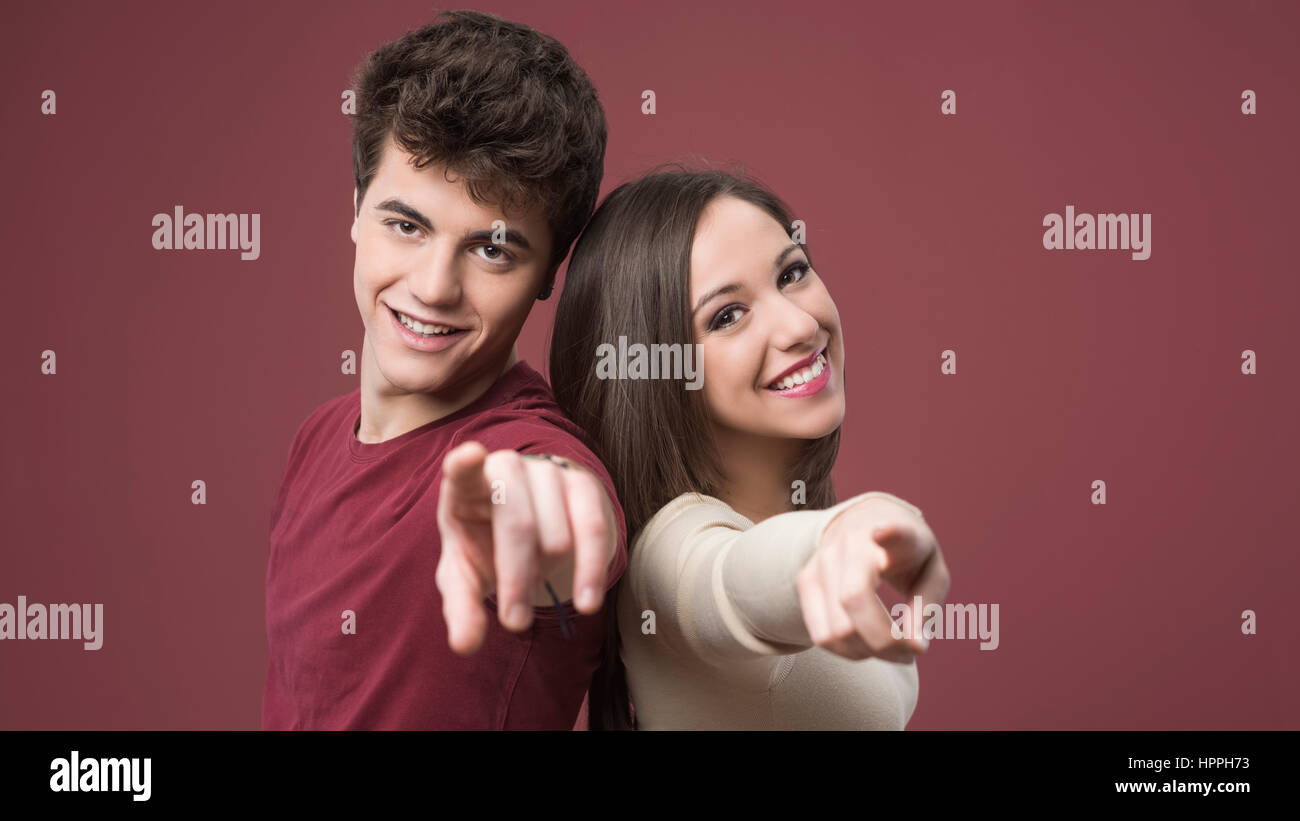 Happy young couple pointing at camera and smiling on red background ...