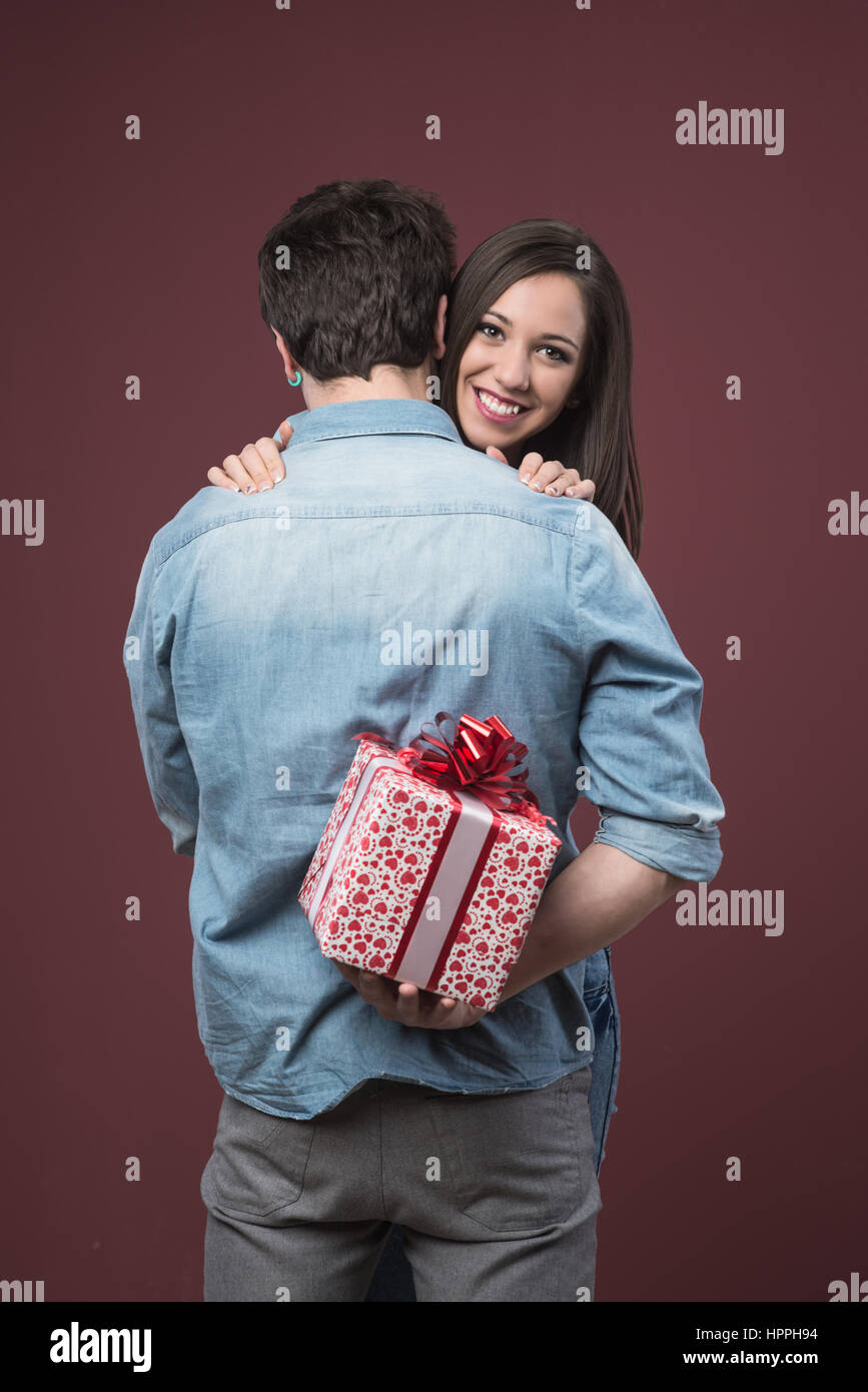Smiling young woman receiving a beautiful gift with red ribbon from her ...