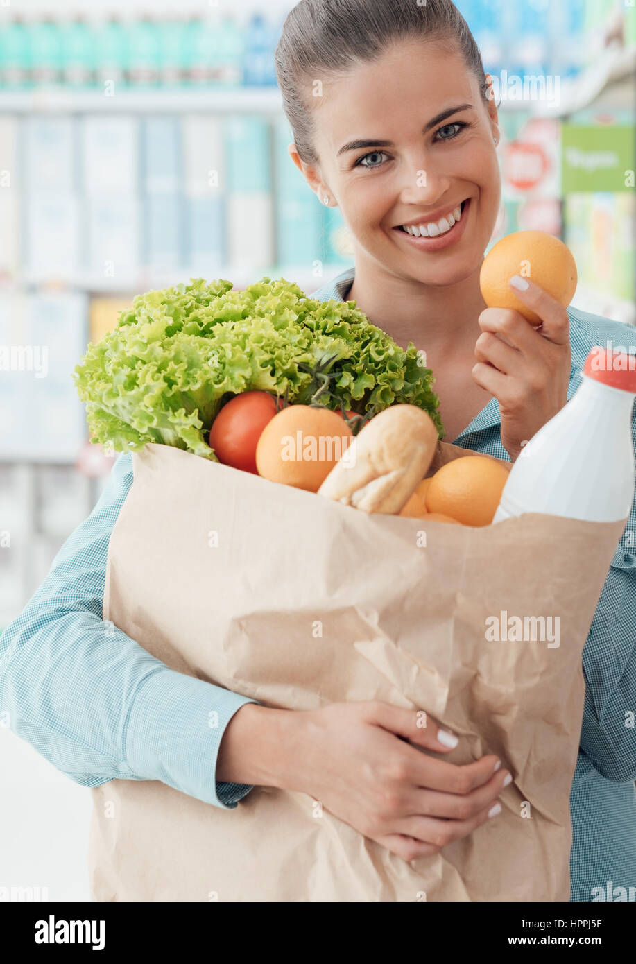Smiling young woman doing grocery shopping at the supermarket, she is ...