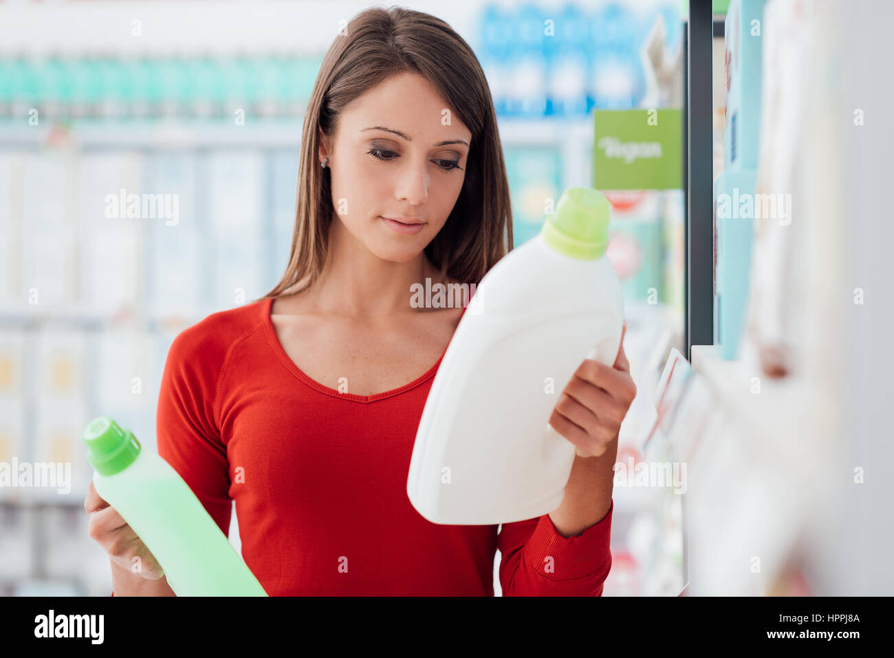 Woman shopping at the supermarket and comparing detergent products, she ...