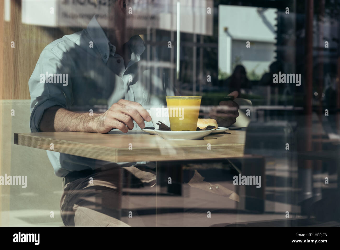Man having breakfast at the cafe next to a window with reflections ...