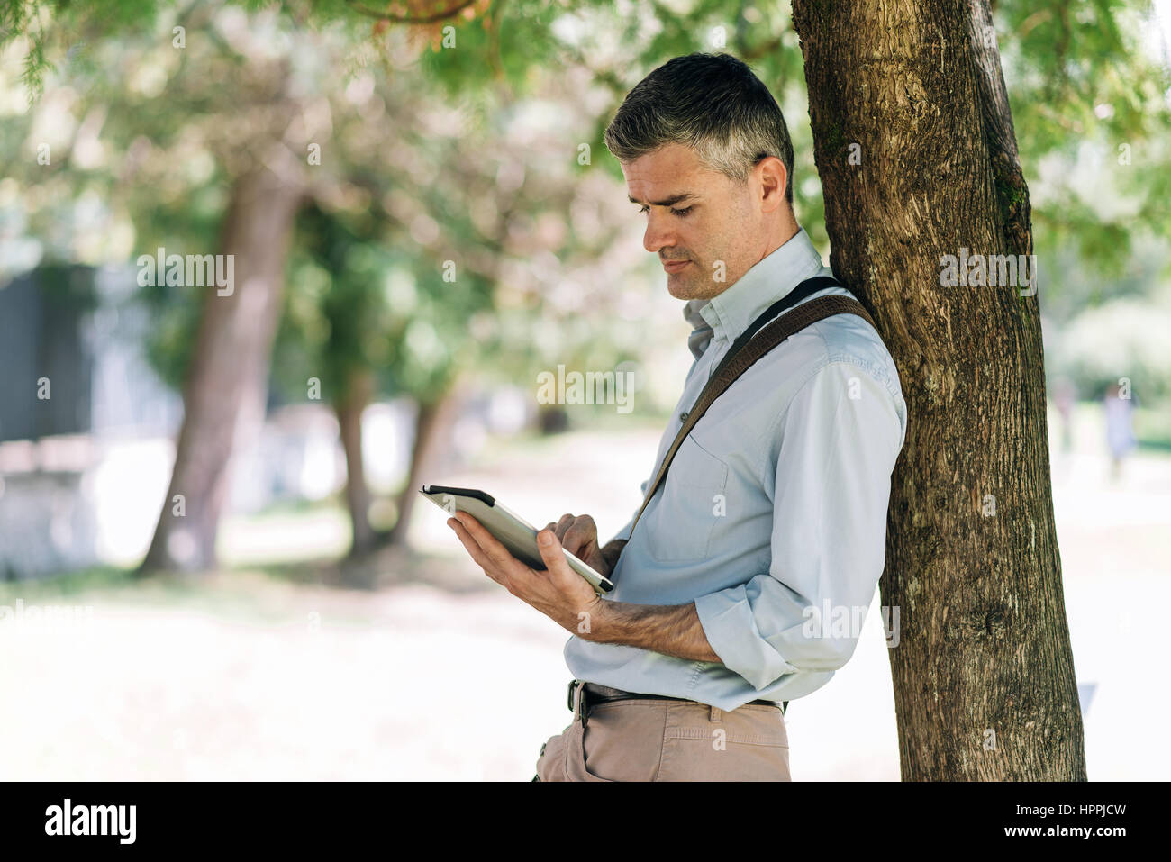 Tourist at the park, he is leaning on a tree and searching for ...