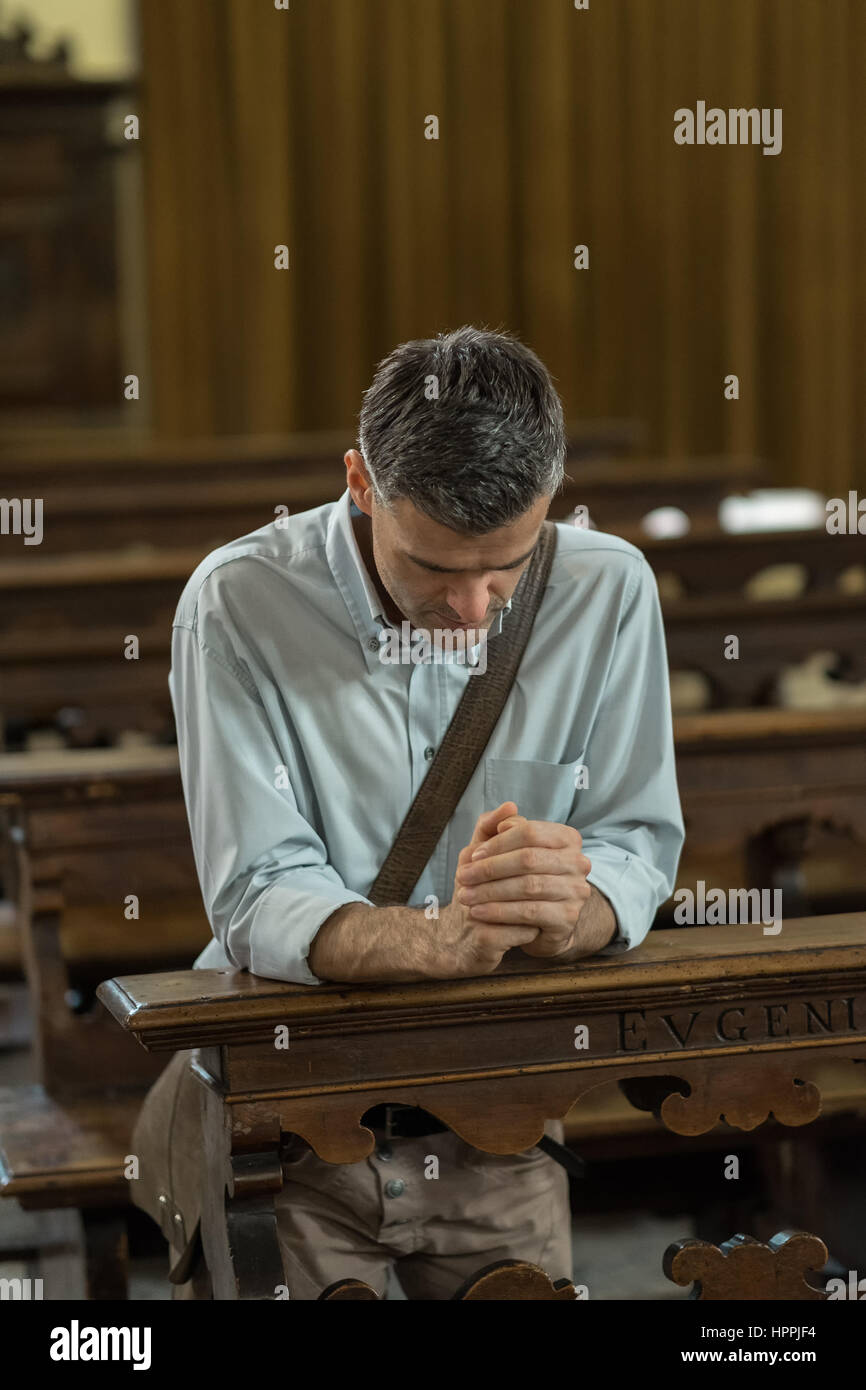 Religious man kneeling at the pew in the Church and praying with hands ...