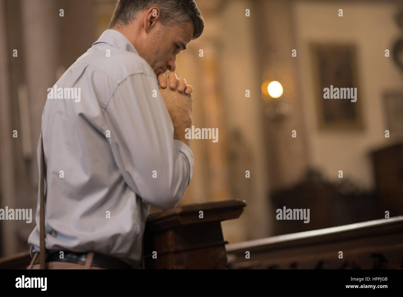 Religious man kneeling at the pew in the Church and praying with hands ...