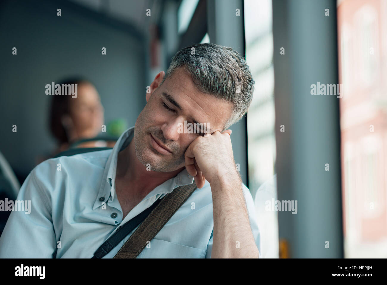 Tired man sitting on the bus and sleeping, he is leaning on his arm ...