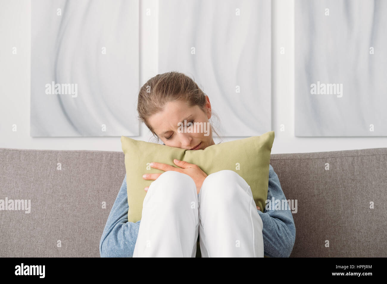 Sad depressed woman at home, she is sitting on the couch and hugging a ...