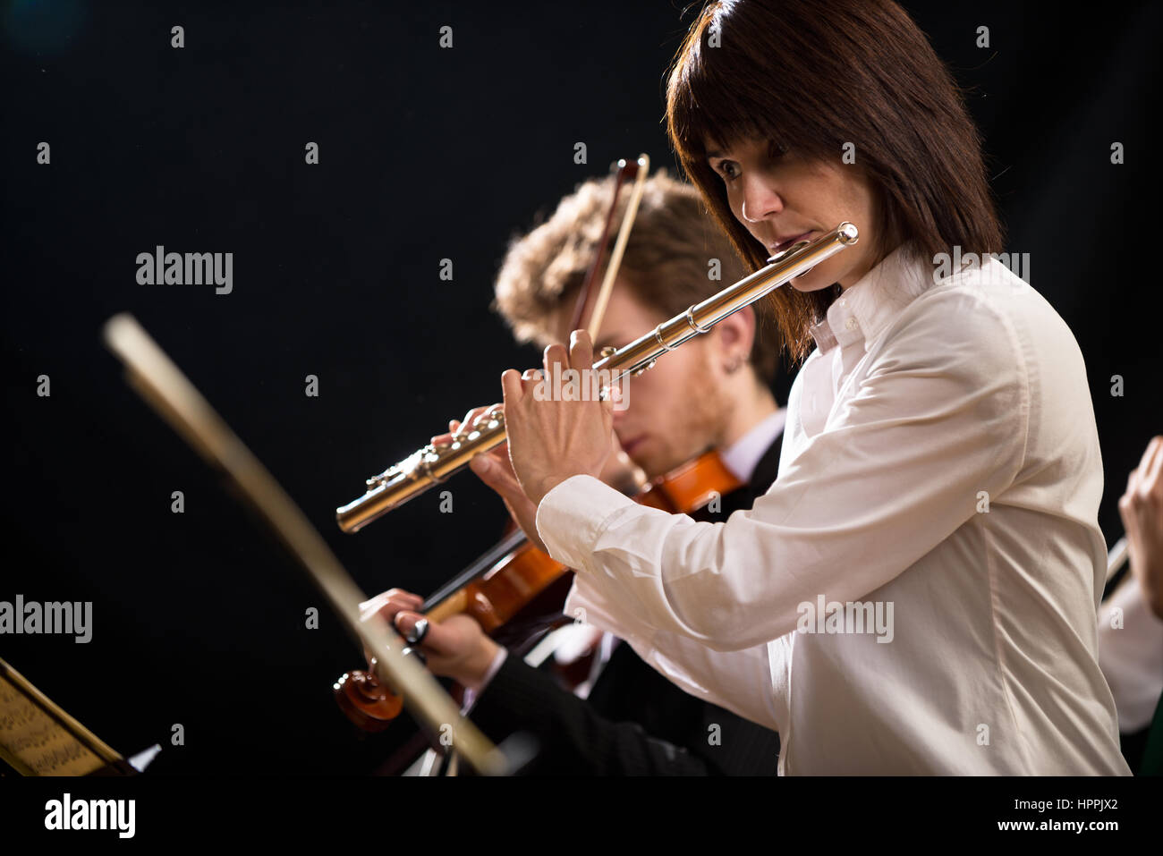 Elegant female flutist performing on stage with orchestra Stock Photo ...