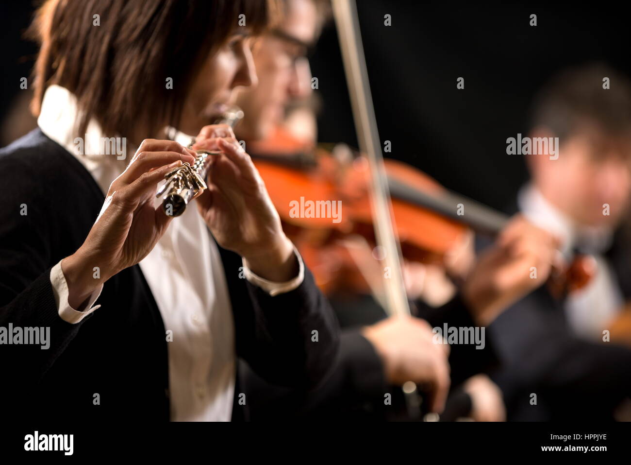 Professional female flutist in concert with symphony orchestra players ...
