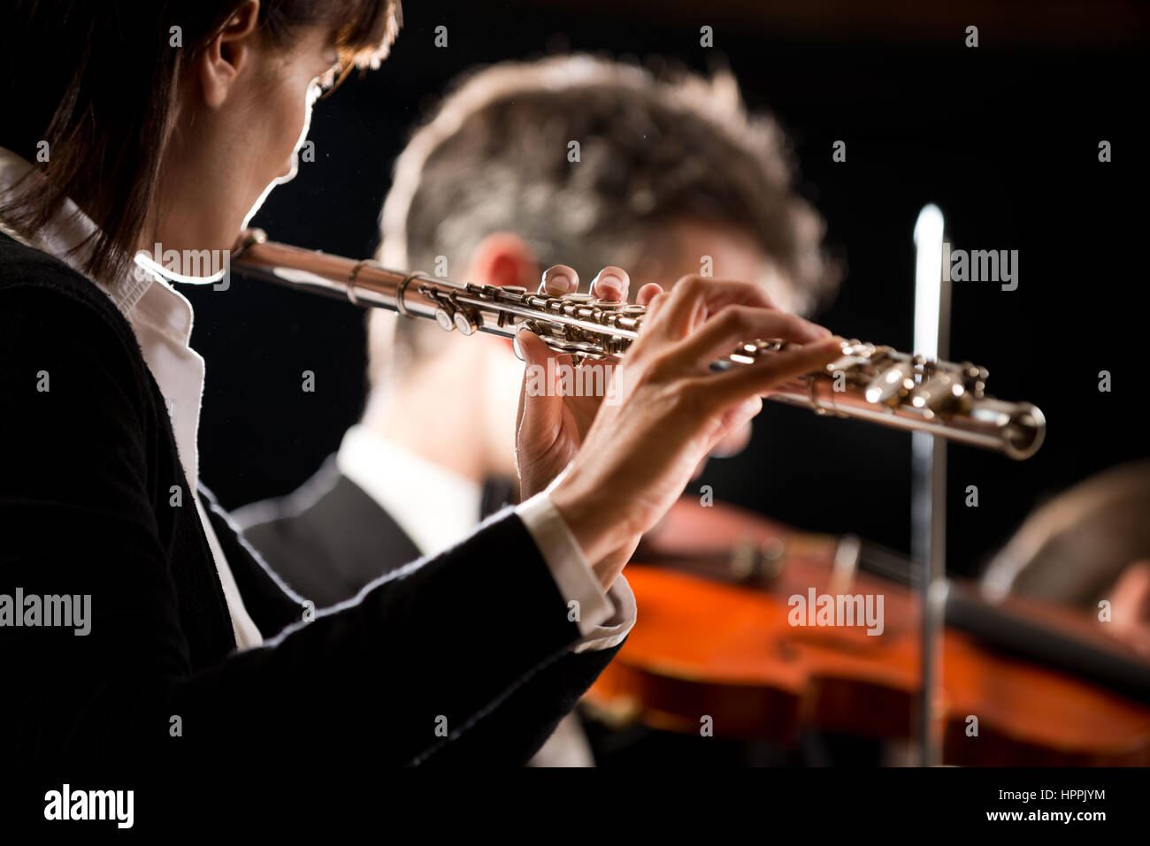 Professional female flutist in concert with symphony orchestra players ...