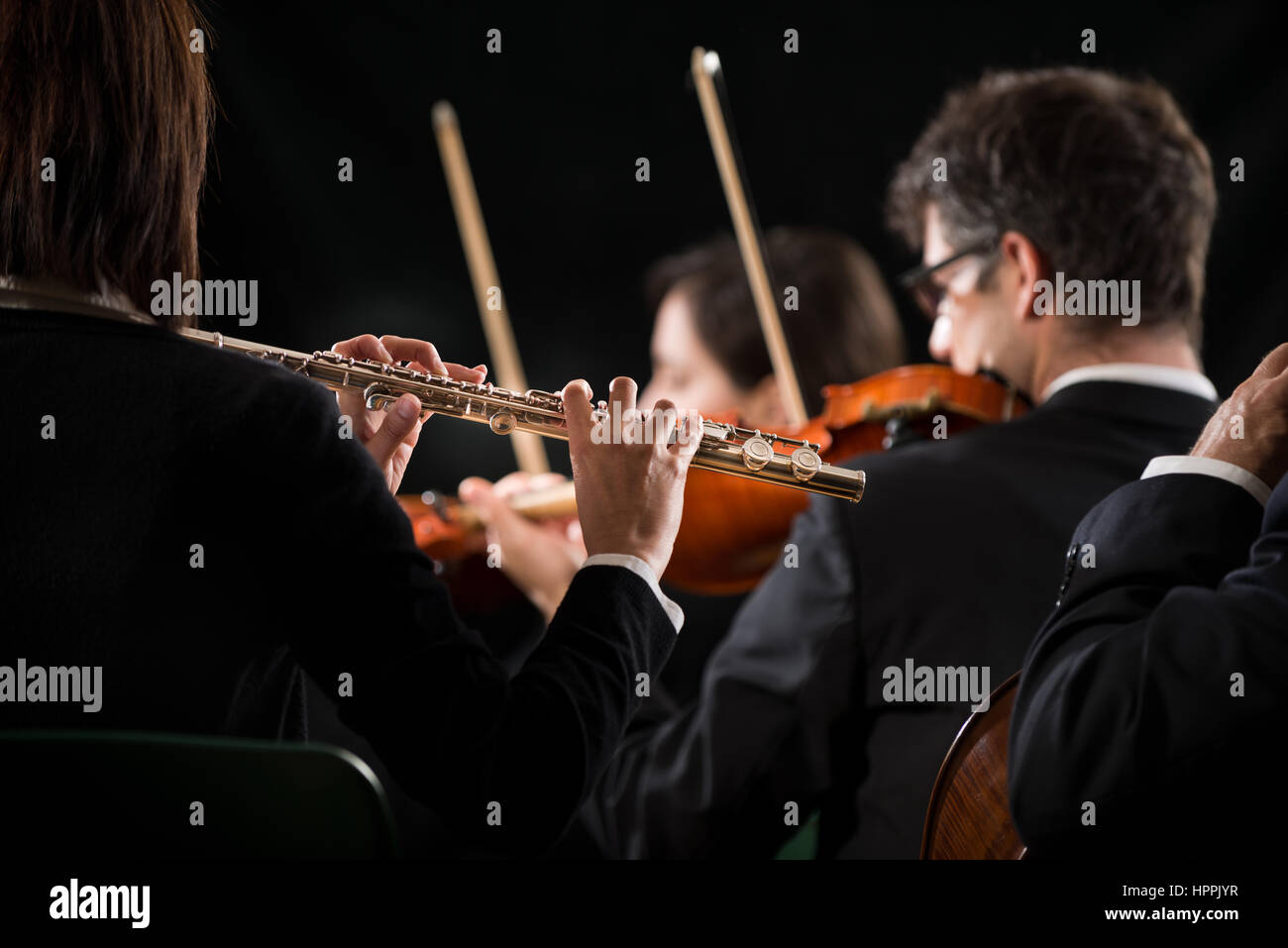 Professional female flutist in concert with symphony orchestra players ...