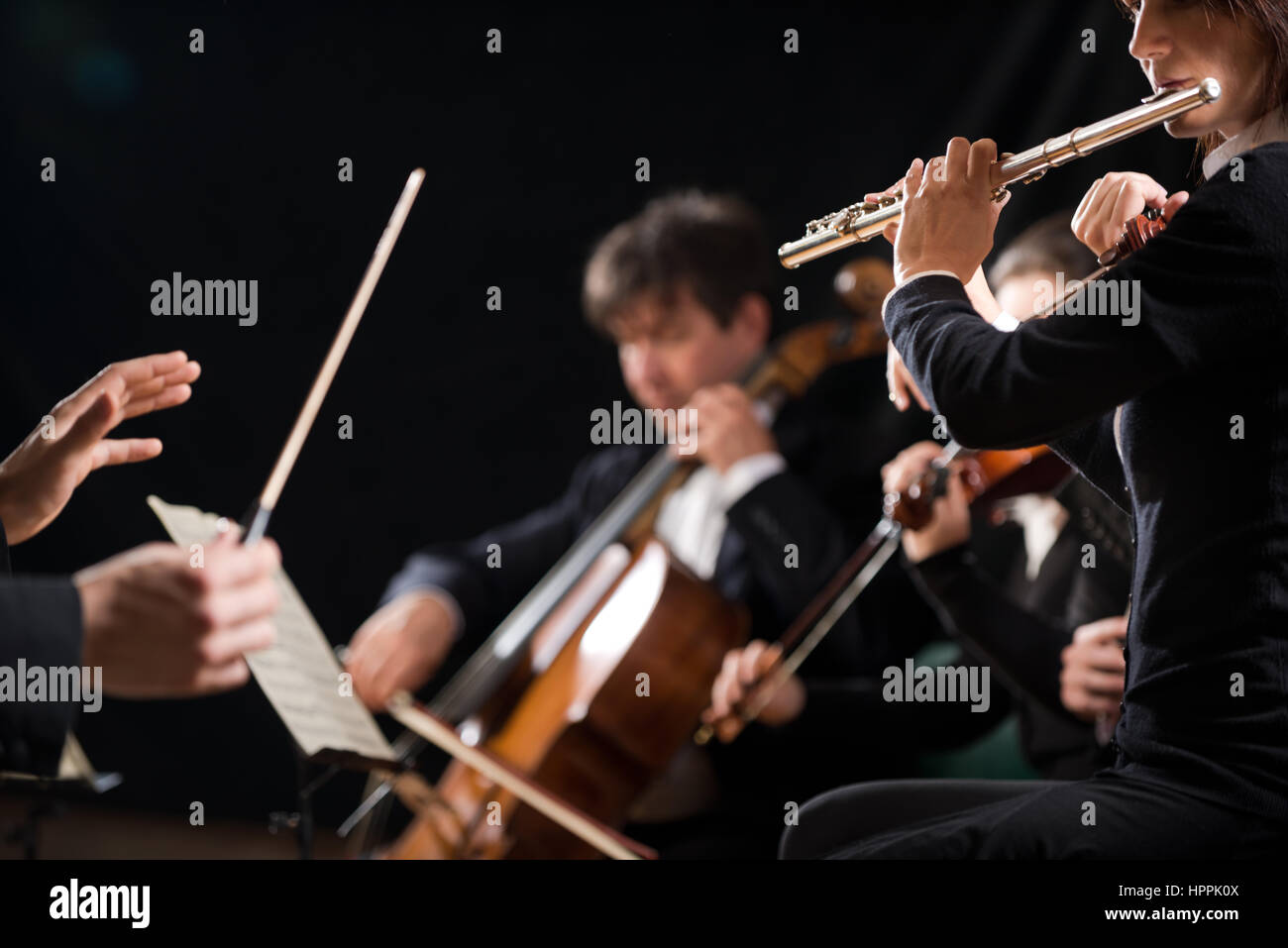 Conductor directing symphony orchestra in concert with flutist on ...