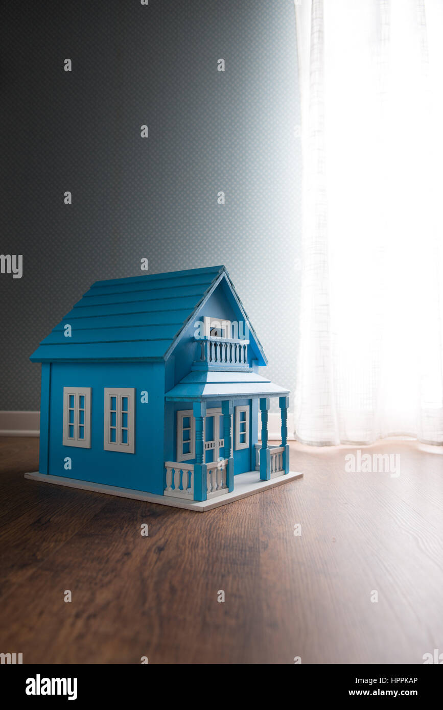 Blue wooden model house next to a window with curtain on wooden floor ...