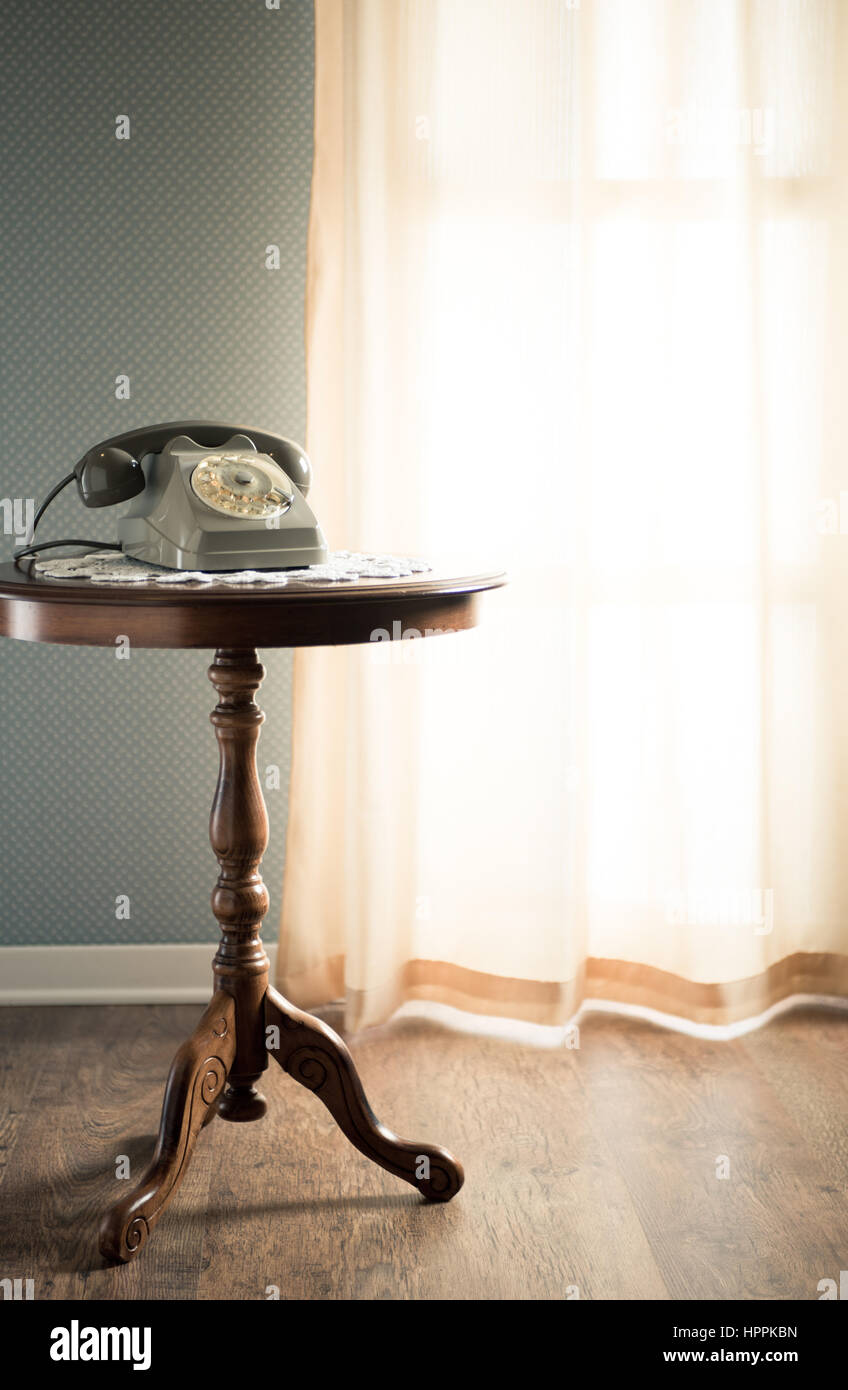 Vintage telephone on doily and wooden table in the living room next to ...
