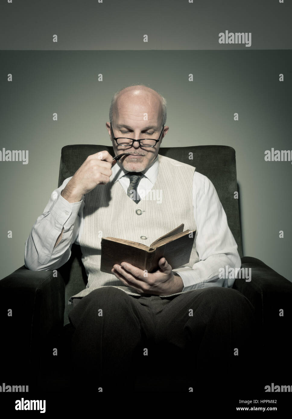 Senior handsome man reading in armchair and smoking pipe Stock Photo ...