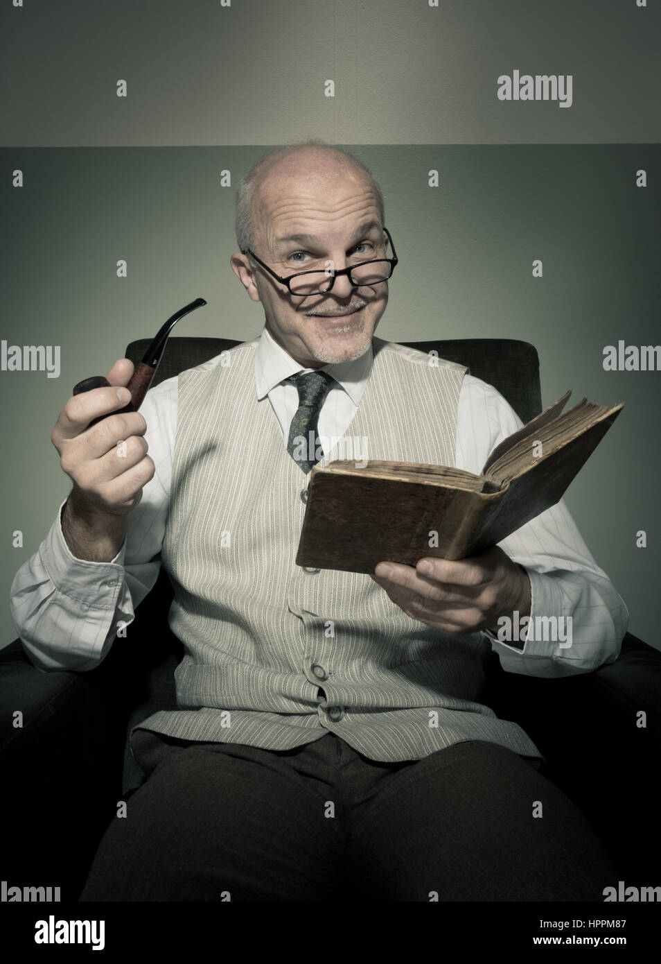 Senior cheerful man reading in armchair and smoking pipe Stock Photo ...