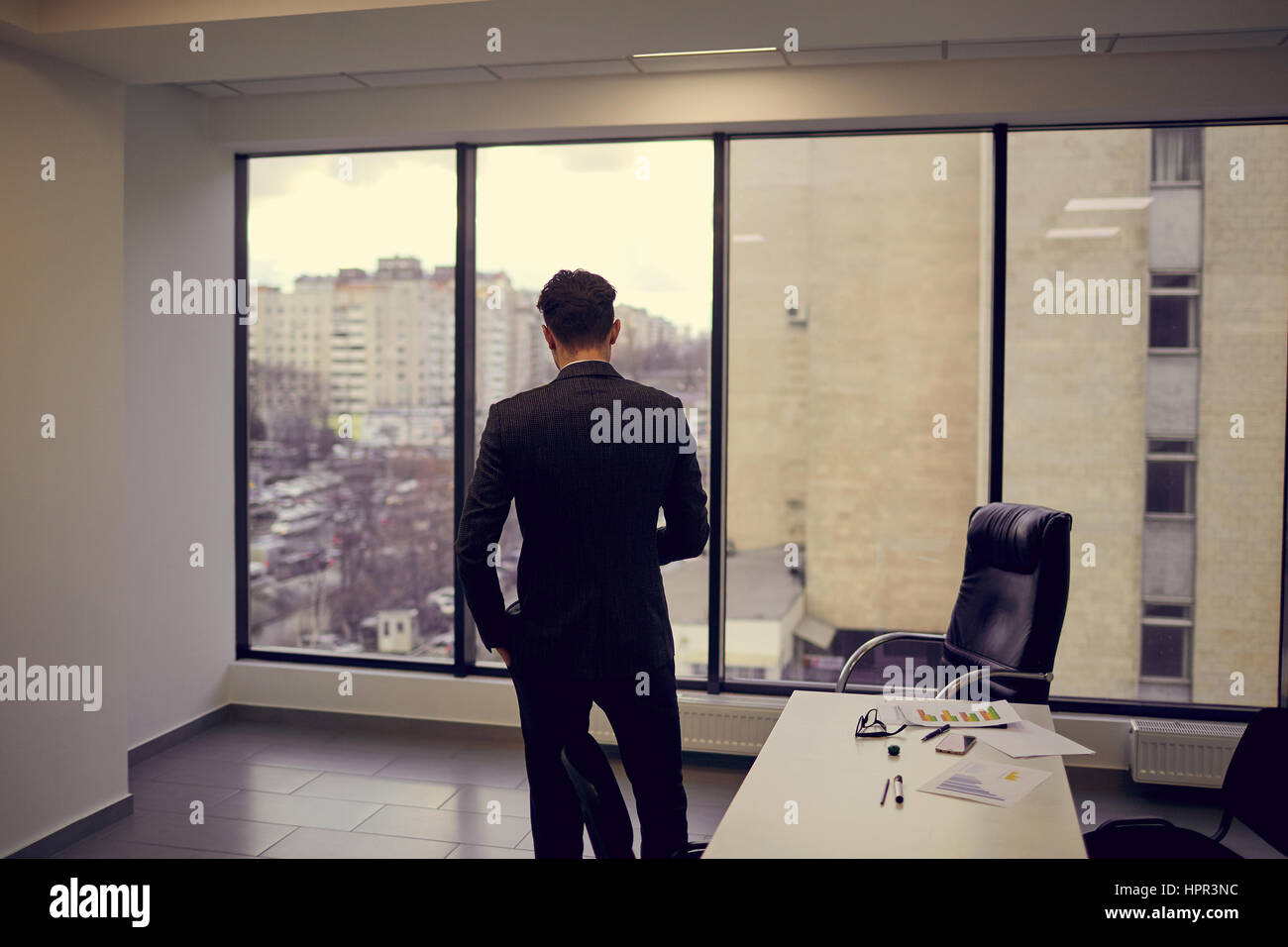 Rear view of a businessman in the office looking out window at night ...