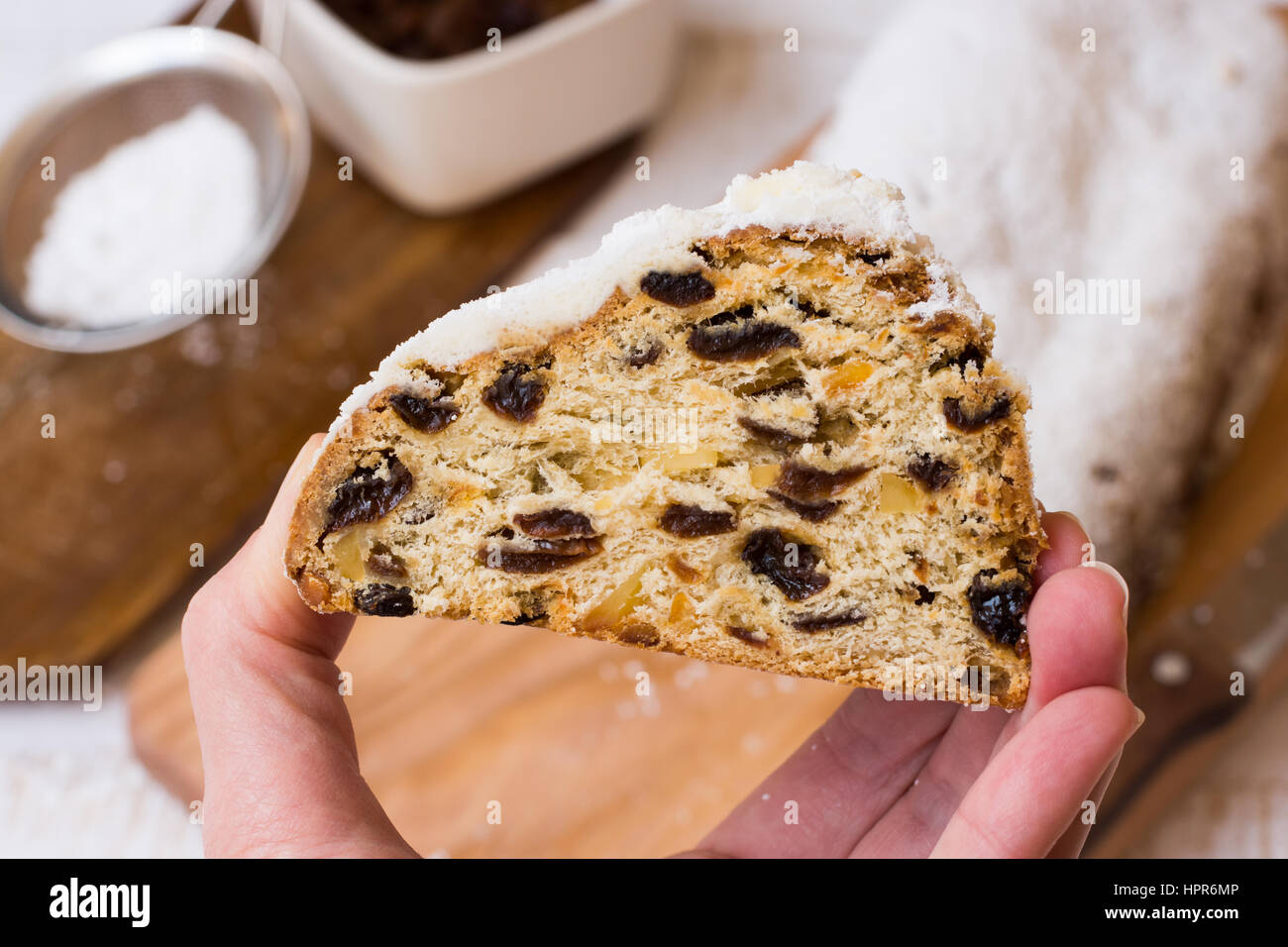 Woman's hand holding a piece of Christmas stollen, loaf and ingredients ...
