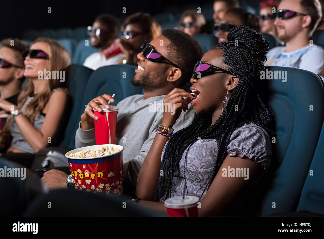 Chilling at the movies. Beautiful African woman in 3D glasses eating ...