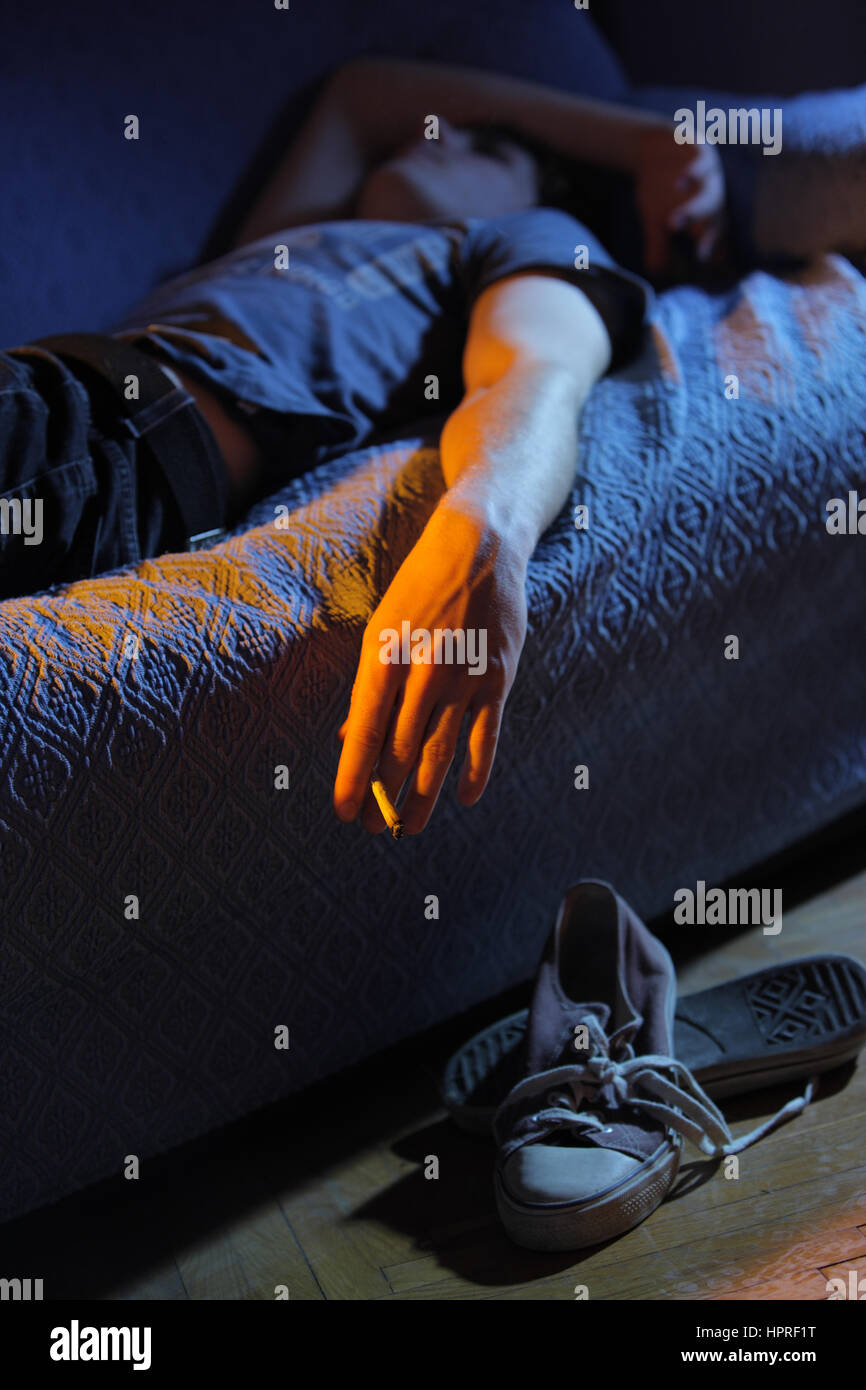 Young man lying on the couch smoking a joint Stock Photo - Alamy