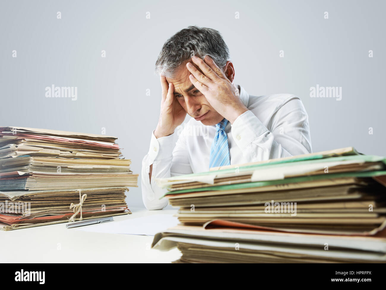 Stressed businessman, with a too much paperwork and files piled up on ...