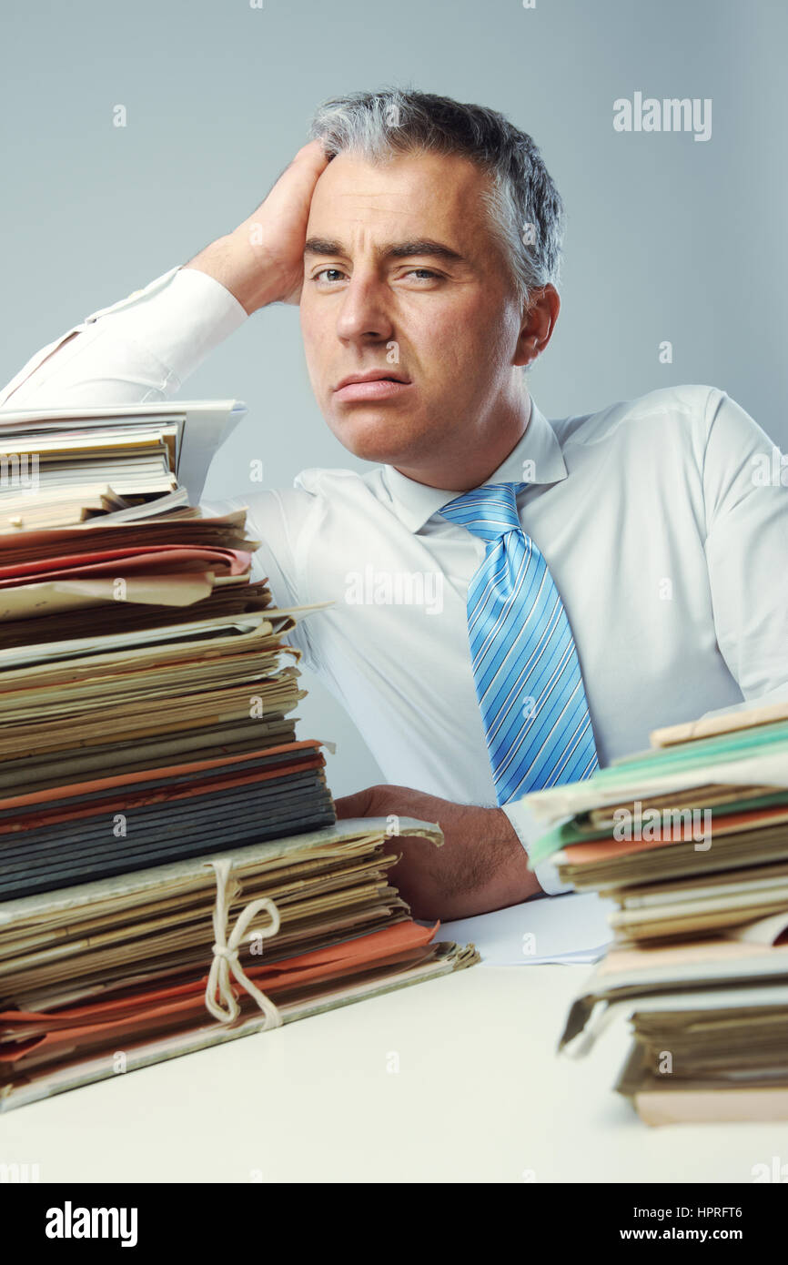 Stressed businessman, with a too much paperwork and files piled up on ...