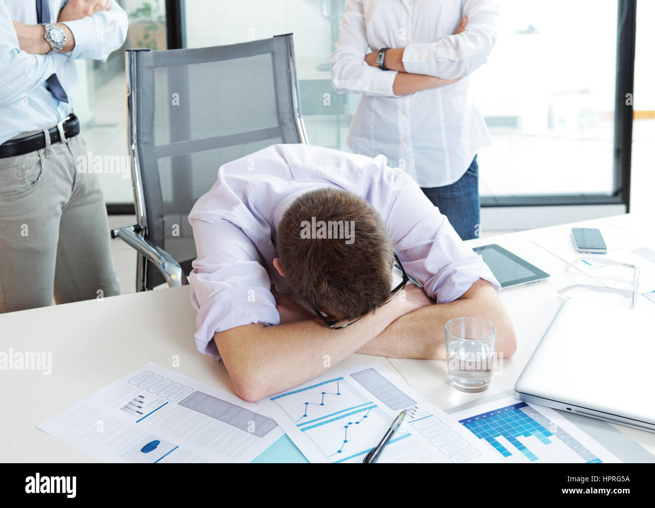 Young office worker is sleeping on the desk, executives behind him ...