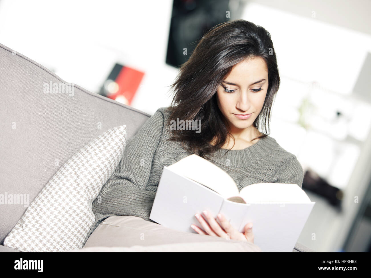 Portrait of a young woman lying on couch with book Stock Photo - Alamy