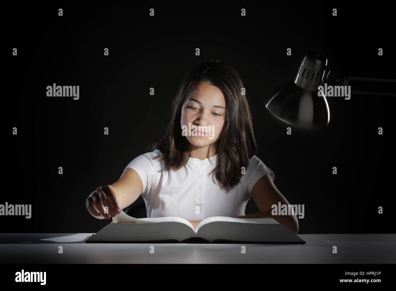 Young girl student, studying late into the night with her book and ...