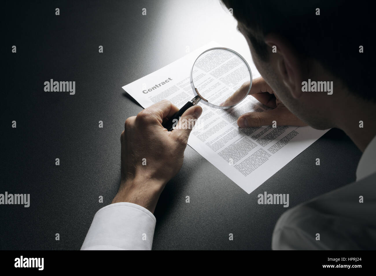 Young businessman looking to a contract through a magnifying glass ...