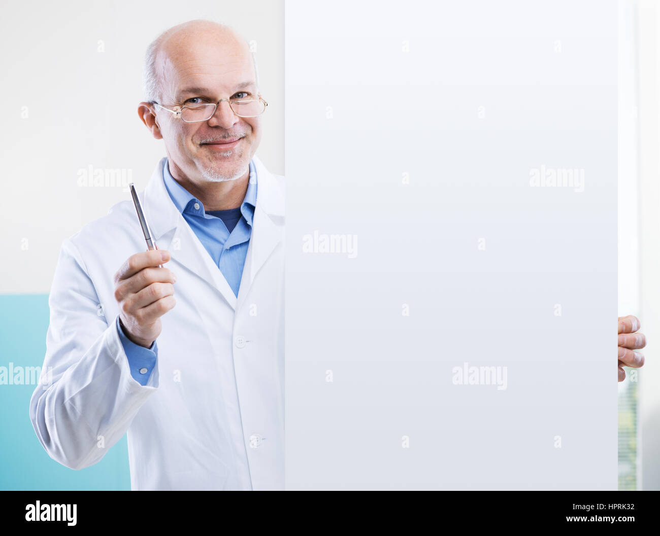 Senior doctor holding a big white sign and pointing with a pen, blank ...